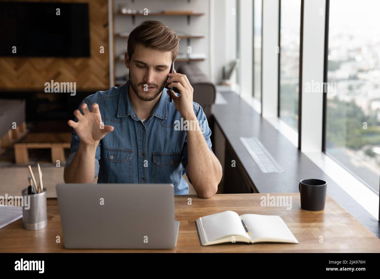 Serious millennial remote employee working at laptop, talking to client ...