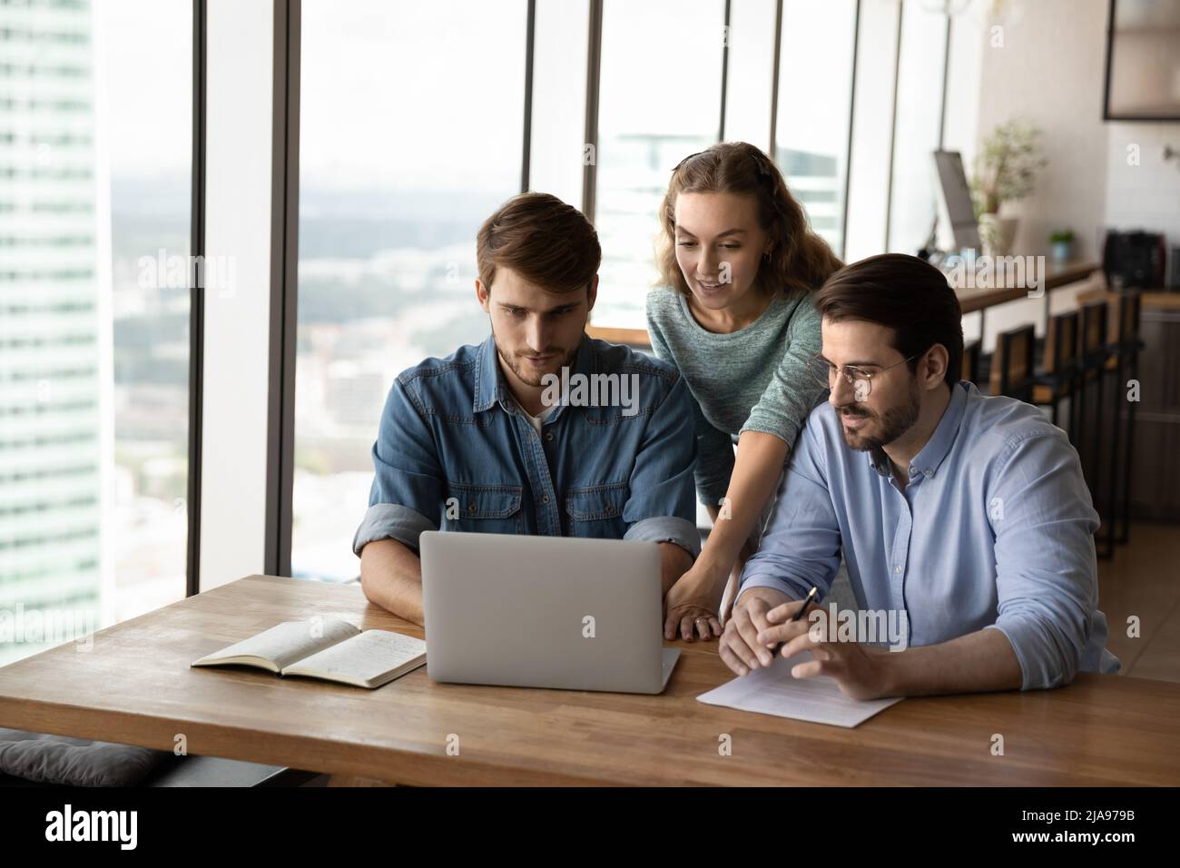 Focused creative group watching virtual presentation on laptop together ...