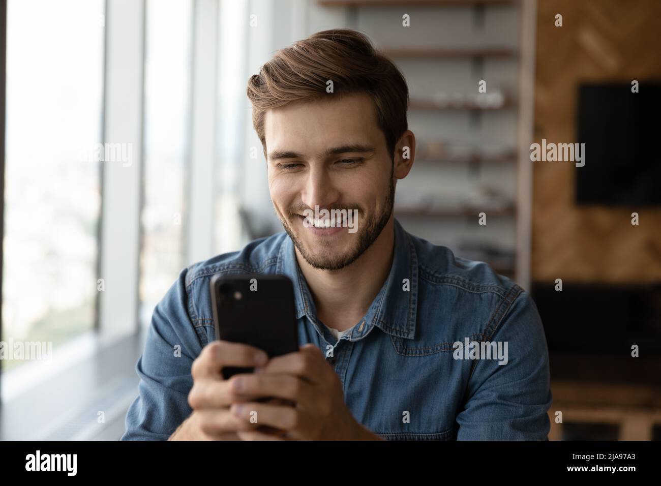 Happy millennial guy using smartphone, reading, texting, smiling at ...