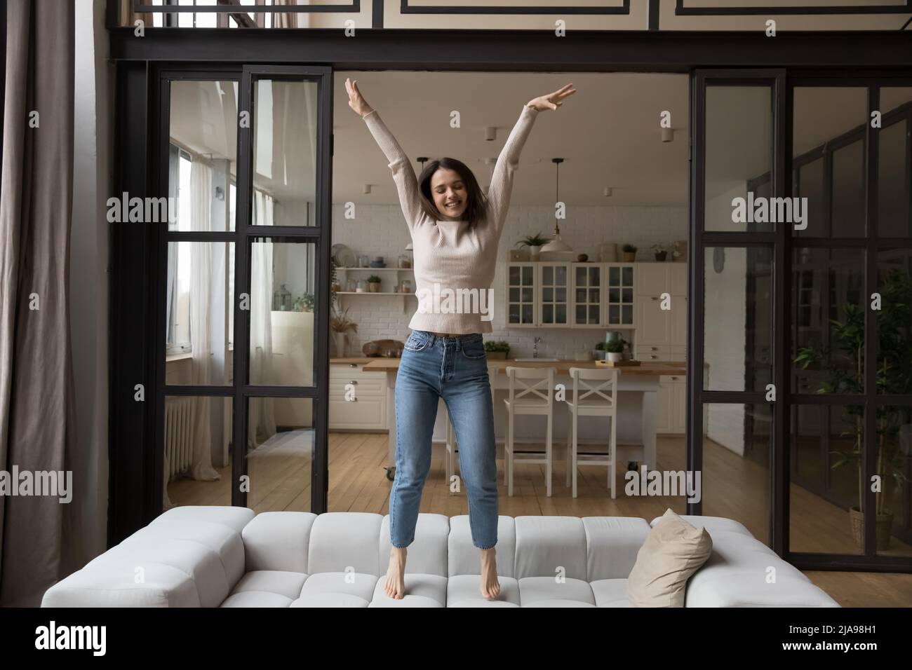 Excited joyful adult dancer girl jumping on sofa at home Stock Photo ...
