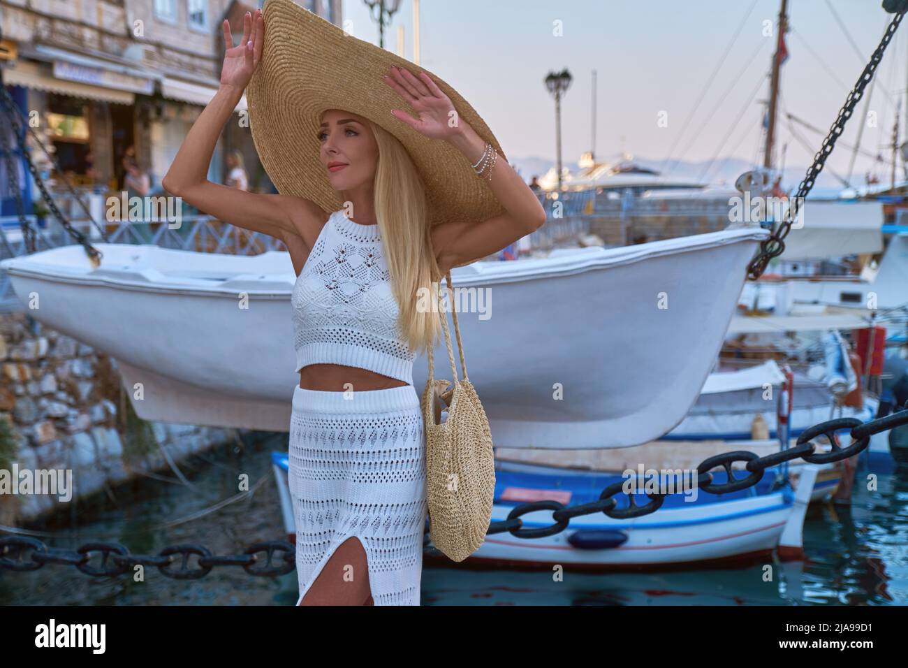 Young lady wearing dress and straw hat walking in marina. Greece, Hydra ...