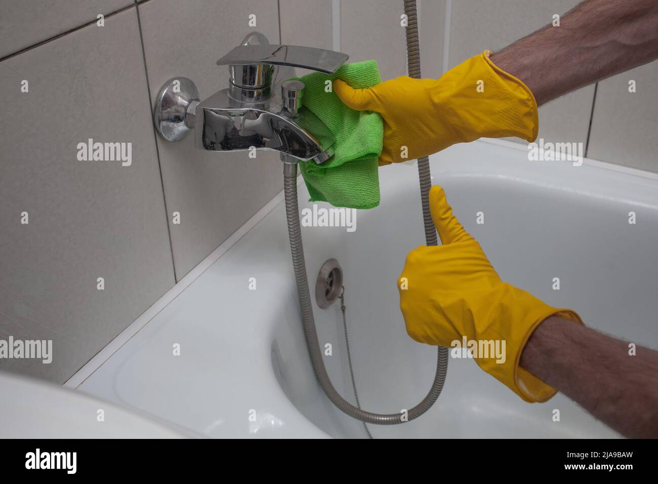 Hands with rag and detergent spray cleaning a faucet in the bathroom ...