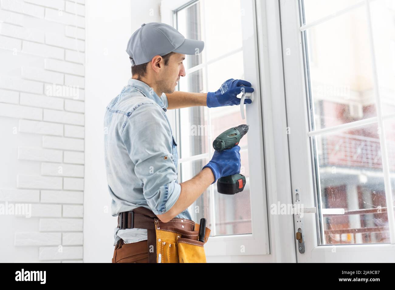 Man fixing lock to window with electric screwdriver Stock Photo - Alamy