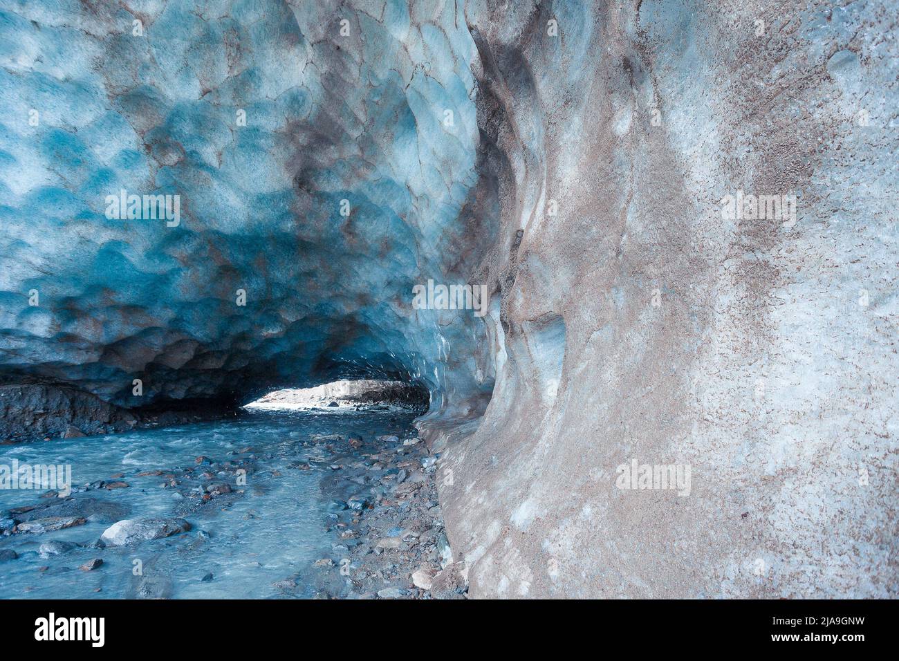Blue cave carved into the Vallelunga glacier ice crossed by a stream ...