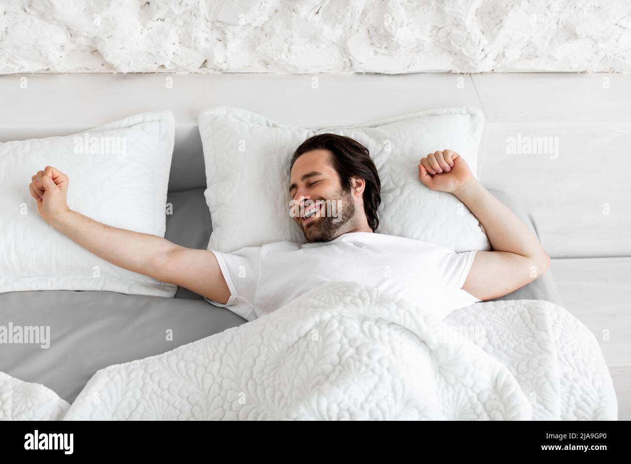 Top view of smiling young man stretching in bed Stock Photo - Alamy