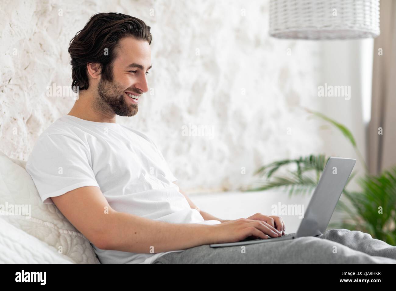Handsome young guy using laptop in bed, working from home Stock Photo ...