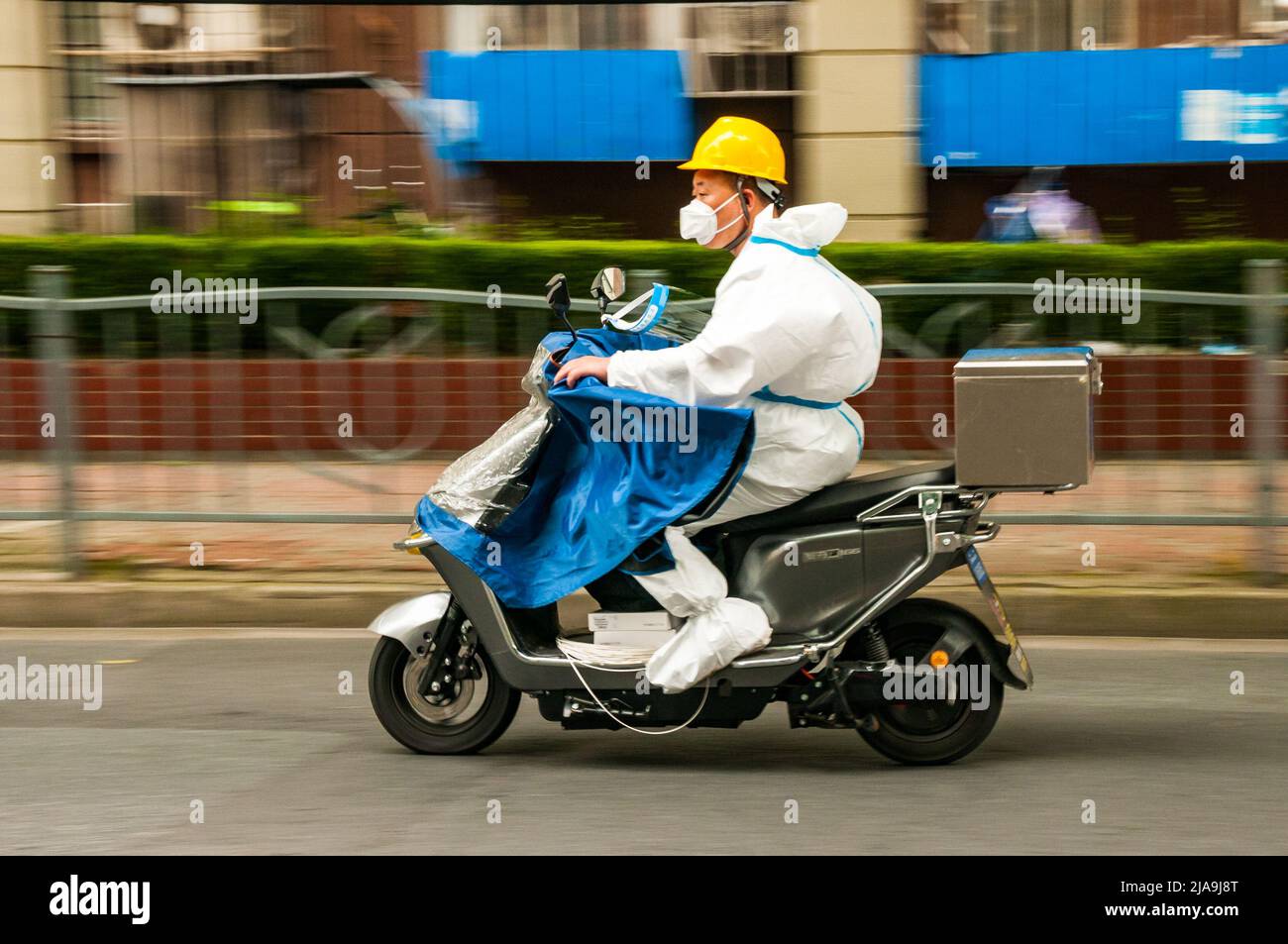 A delivery rider wearing white PPE gear speeds past on a scooter in ...