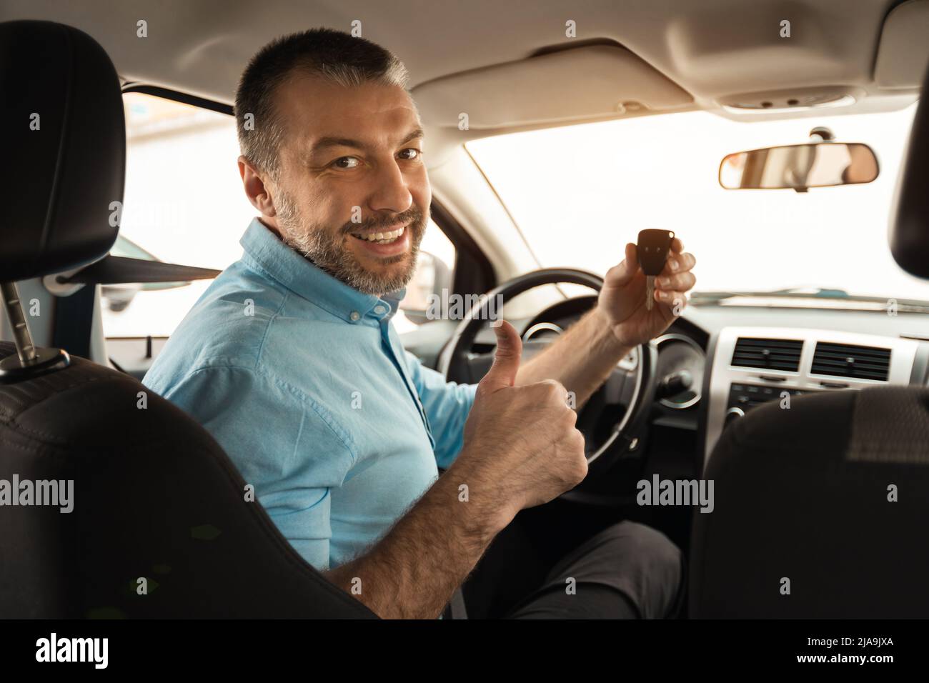 Happy man sitting in car showing keys gesturing thumbs up Stock Photo ...