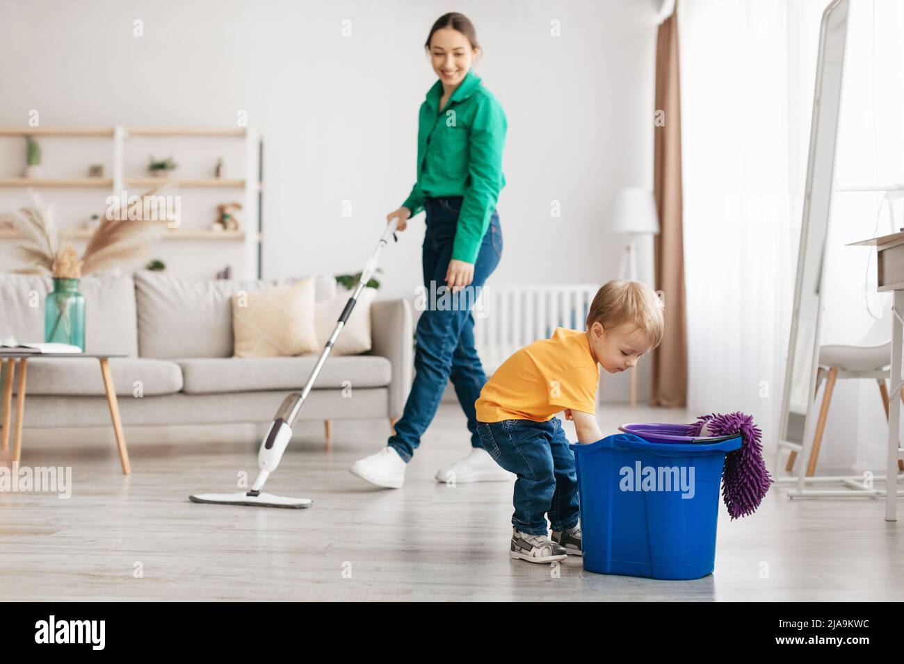 Little boy helping young mother cleaning at home, child getting rag out ...