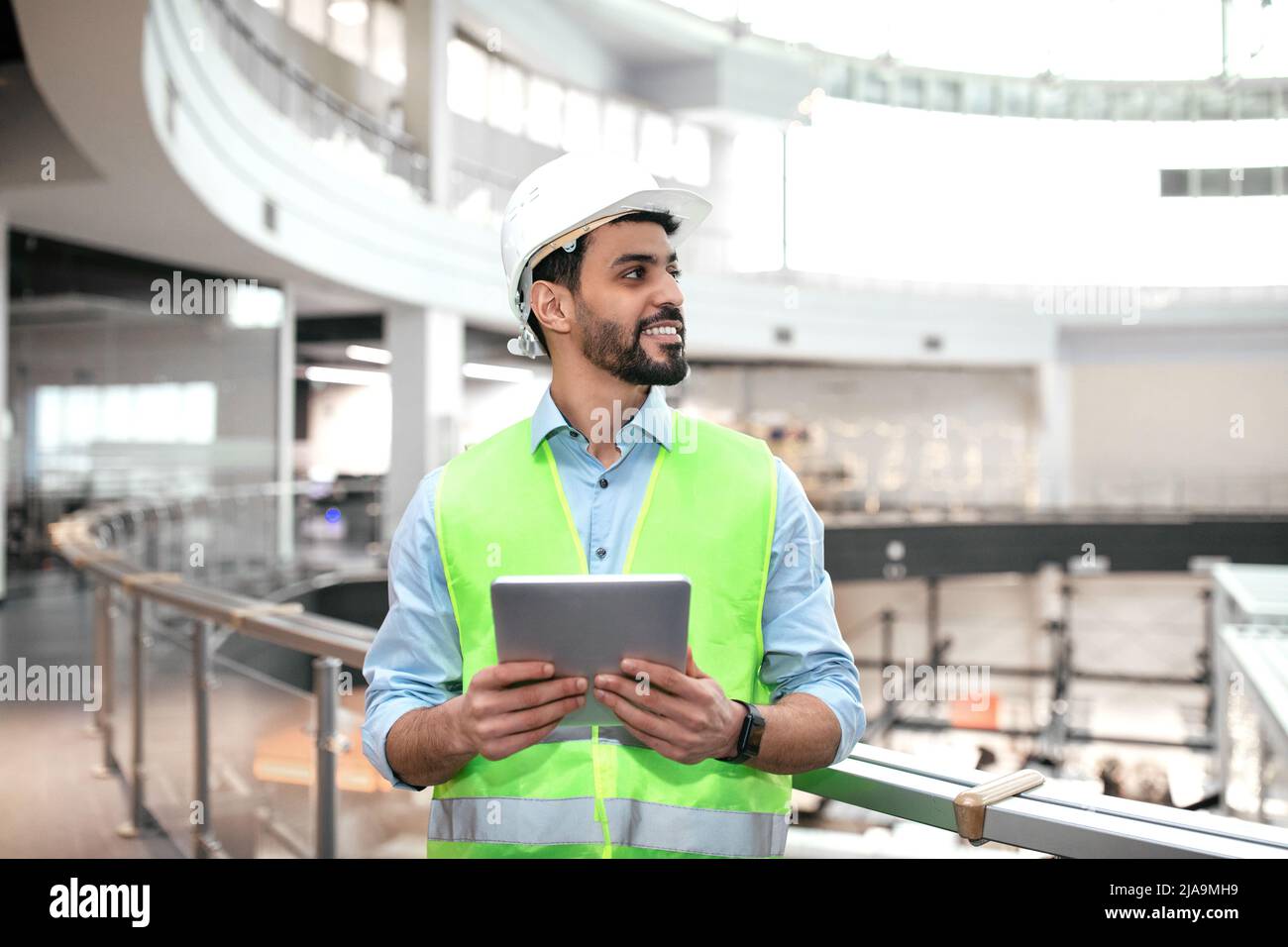 Cheerful millennial muslim engineer guy in protective uniform, hard hat ...