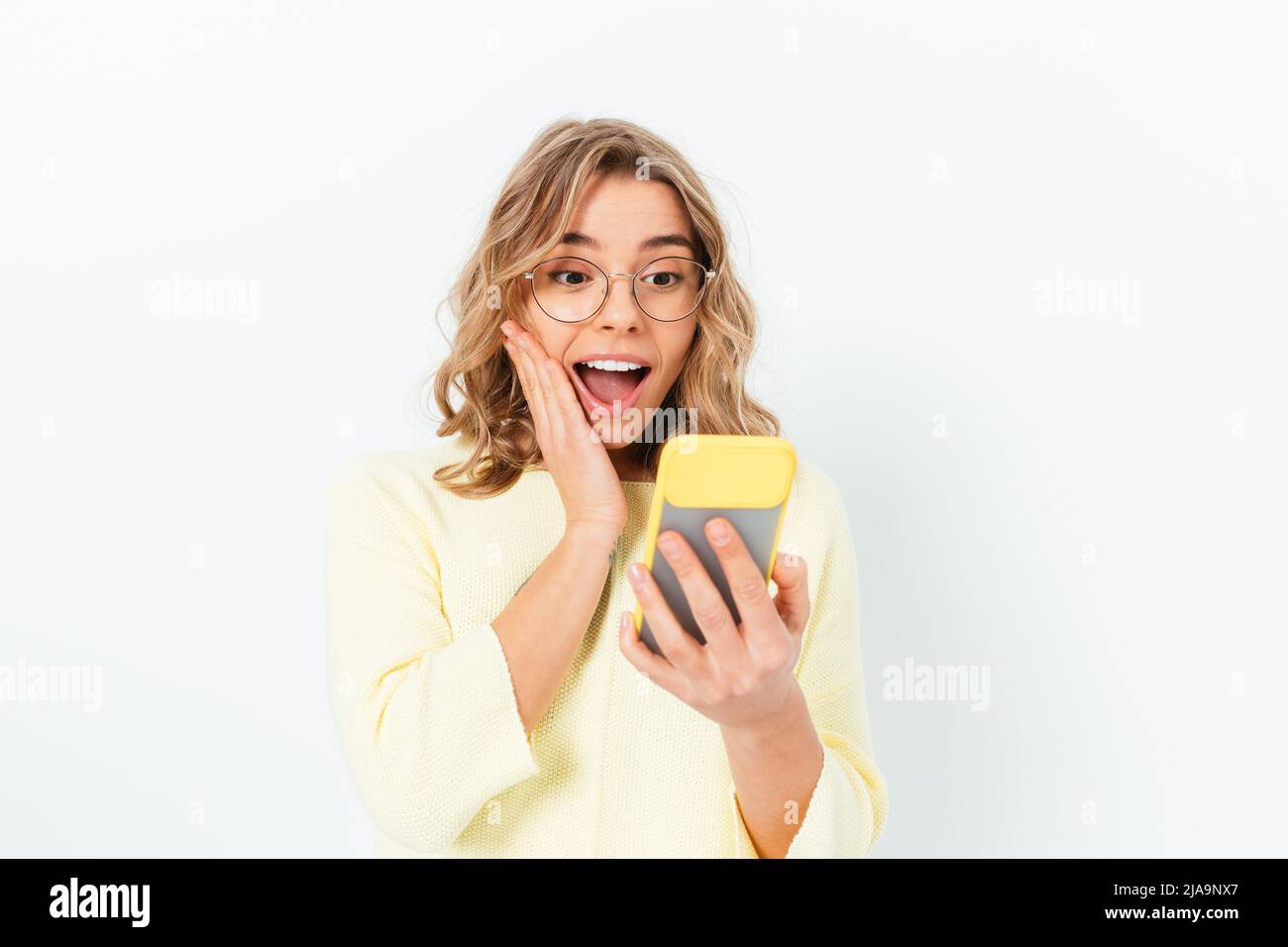 Happy dazed young woman looking into her smartphone while standing ...