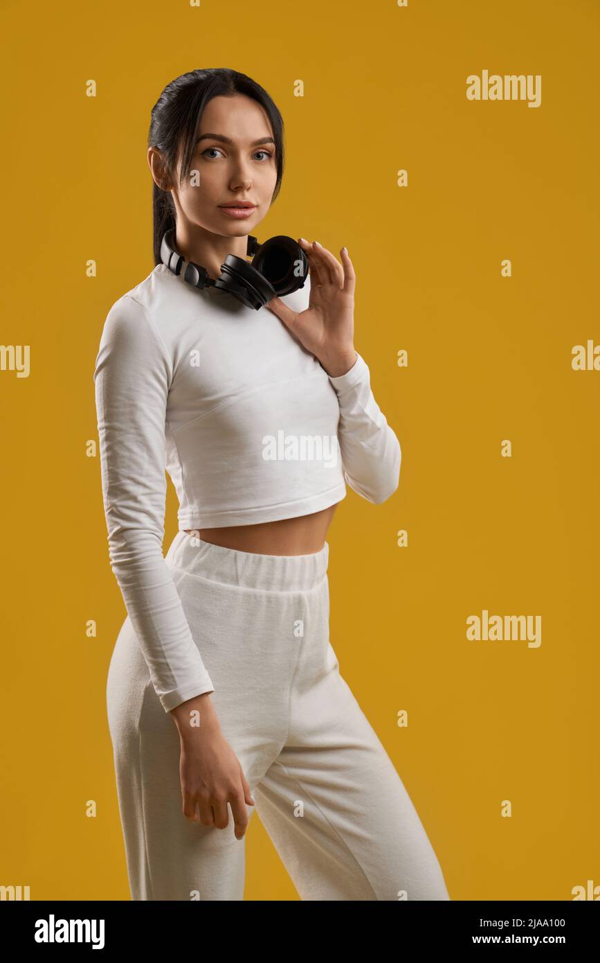 Cute woman in white outfit with wireless headphones looking at camera ...