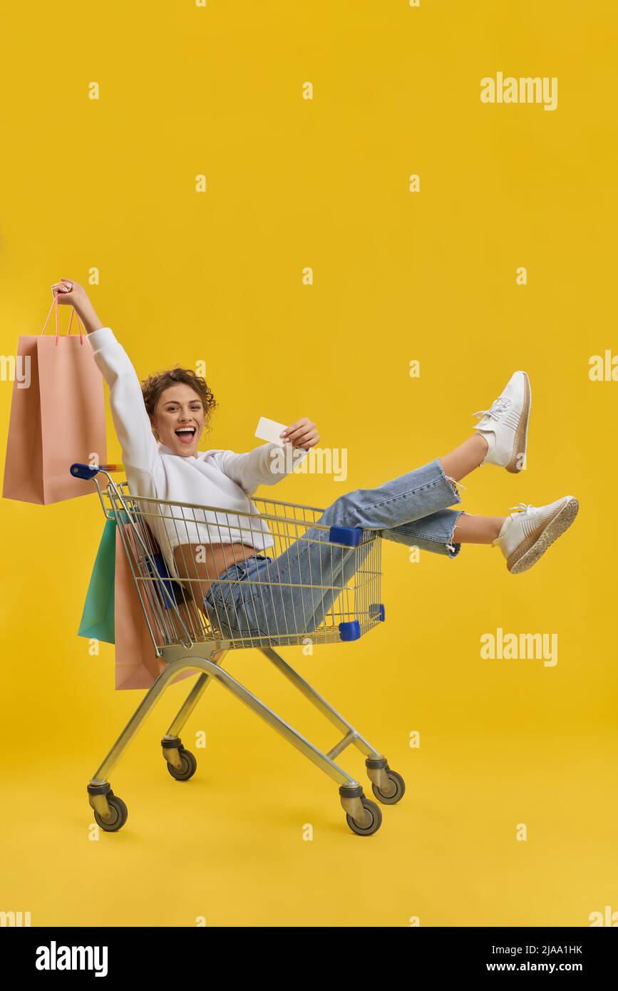Happy lady holding credit card, while riding in shopping trolley in ...