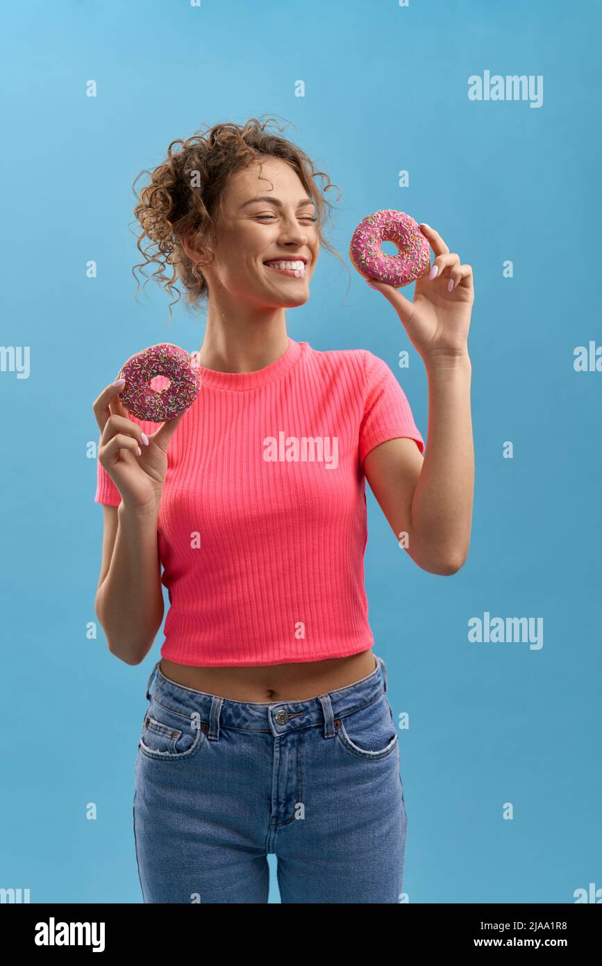 Cheerful woman in casual outfit, holding colorful donuts, smiling ...
