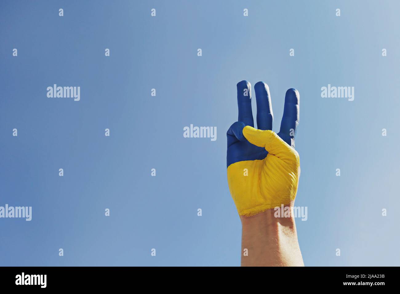 Man's hand lit by sunshine painted in colors of Ukrainian national flag ...