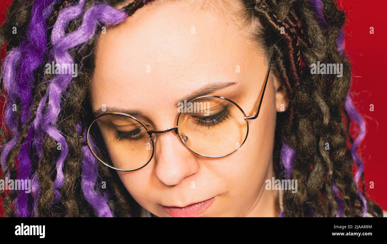 Portrait of young woman in glasses with brown, purple dreadlocks. Close ...