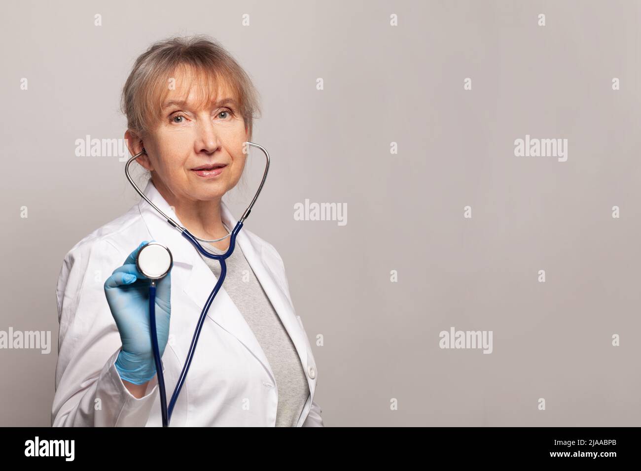 Mature woman doctor in medical uniform standing and holding stethoscope ...