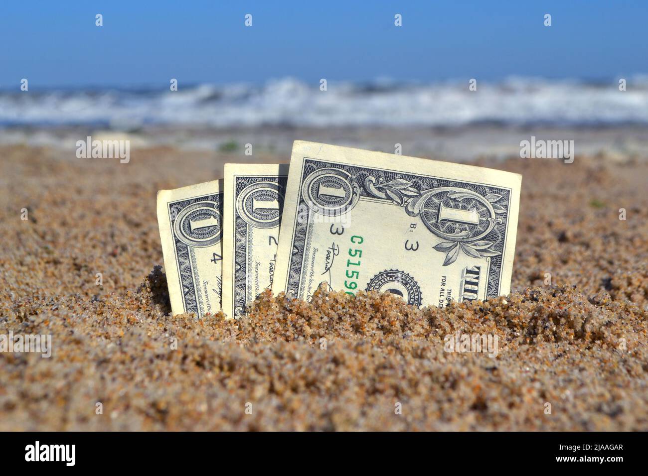 Paper bills one dollar buried in the sand on the beach against backdrop ...