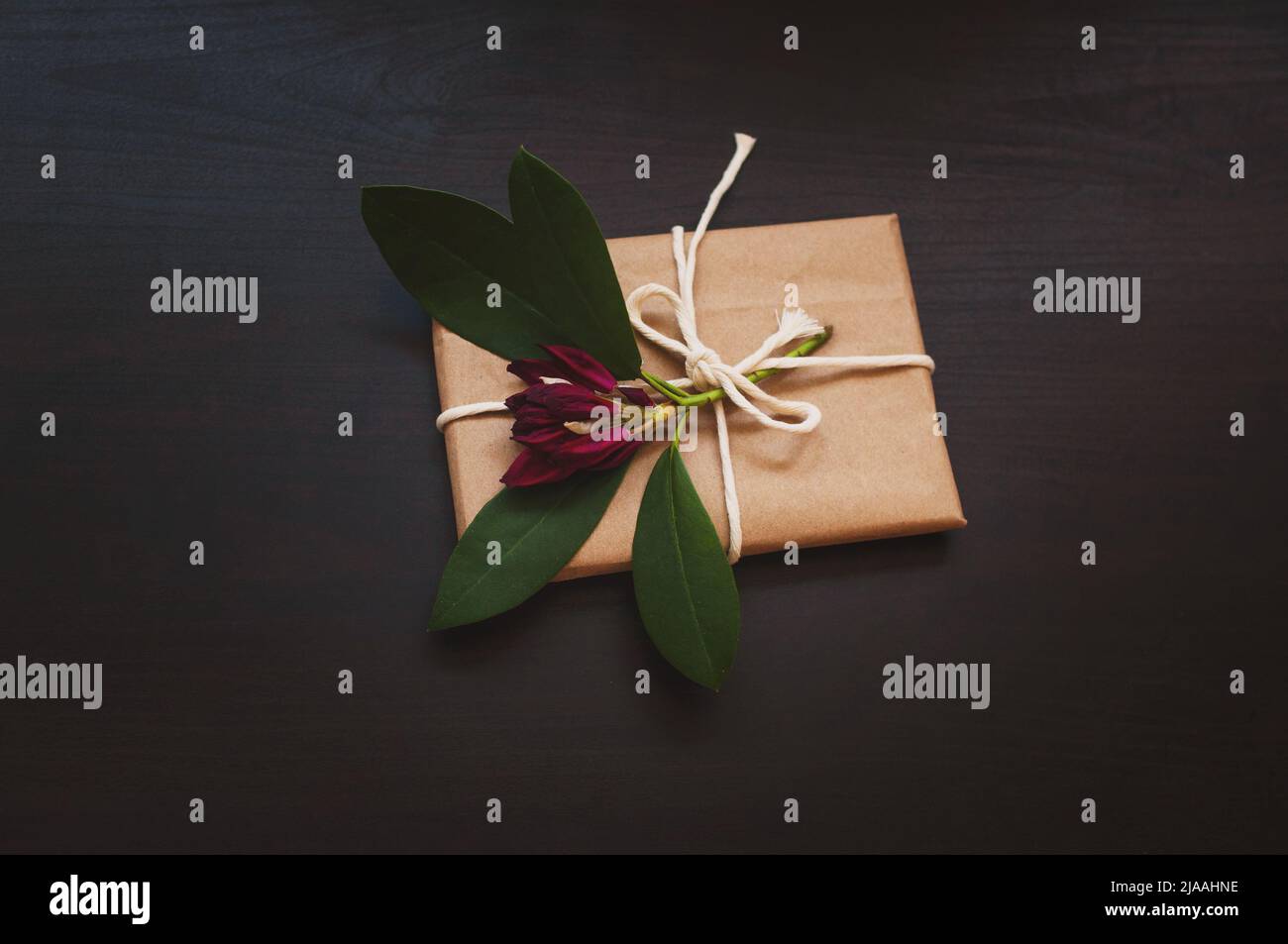 Gift box in craft packaging on wooden black background with purple ...