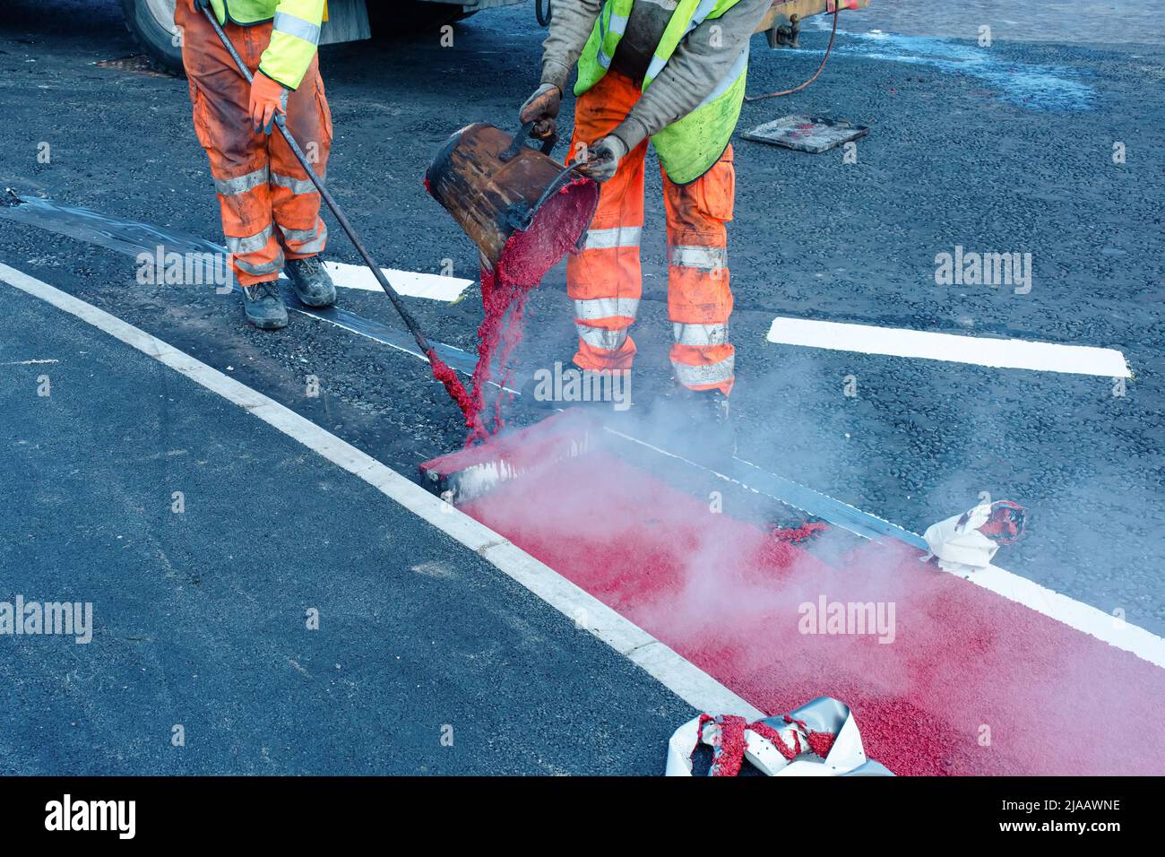 Road workers applying hot red road marking paint on new build road ...