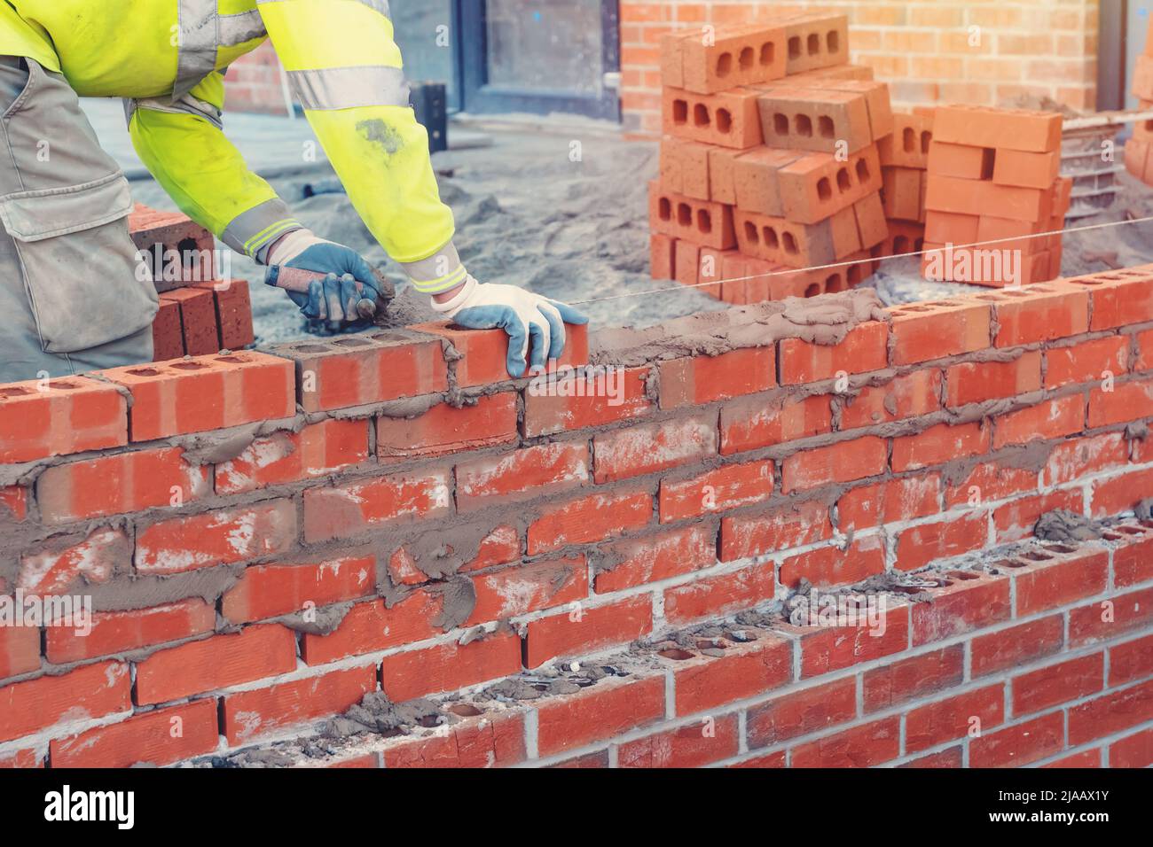 Bricklayer in safety vest and a helmet laying a brick wall using a ...