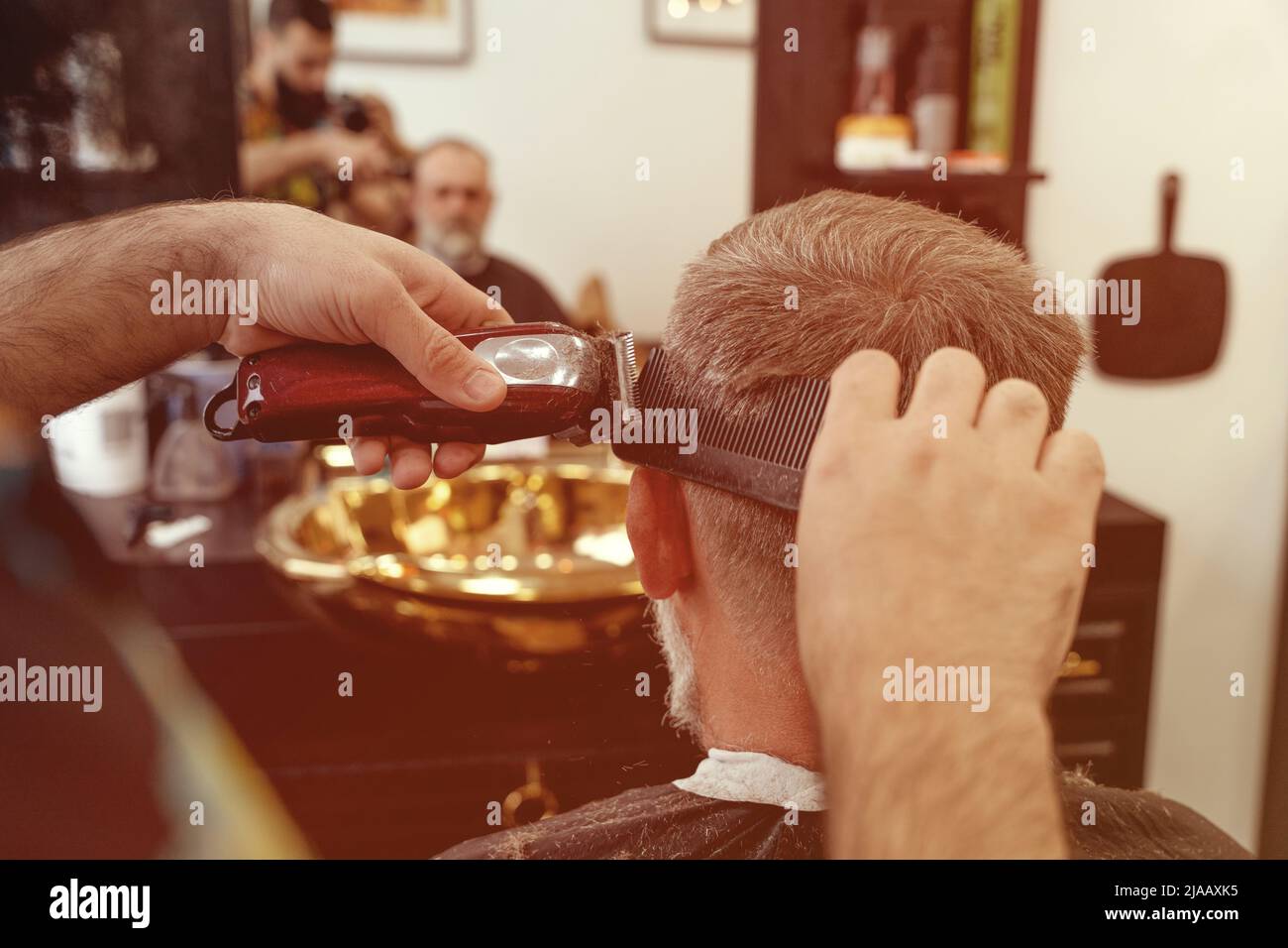 An old man enjoing haircut by a master in a barbershop. An old man gets ...