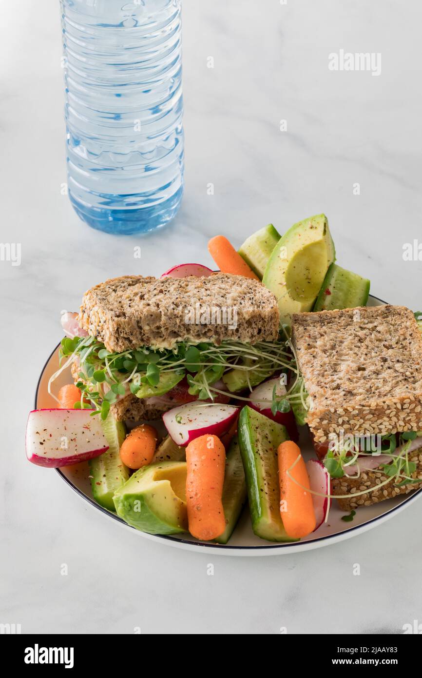Whole grain sandwich with fresh cut raw vegetables and a bottle of ...