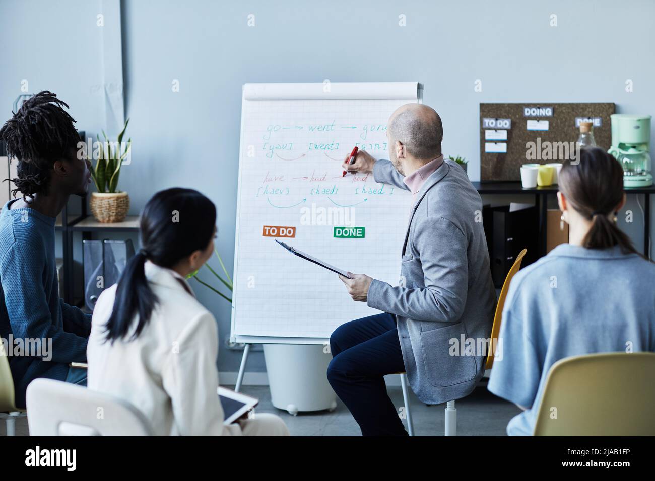 Portrait of male teacher writing on whiteboard while giving English ...