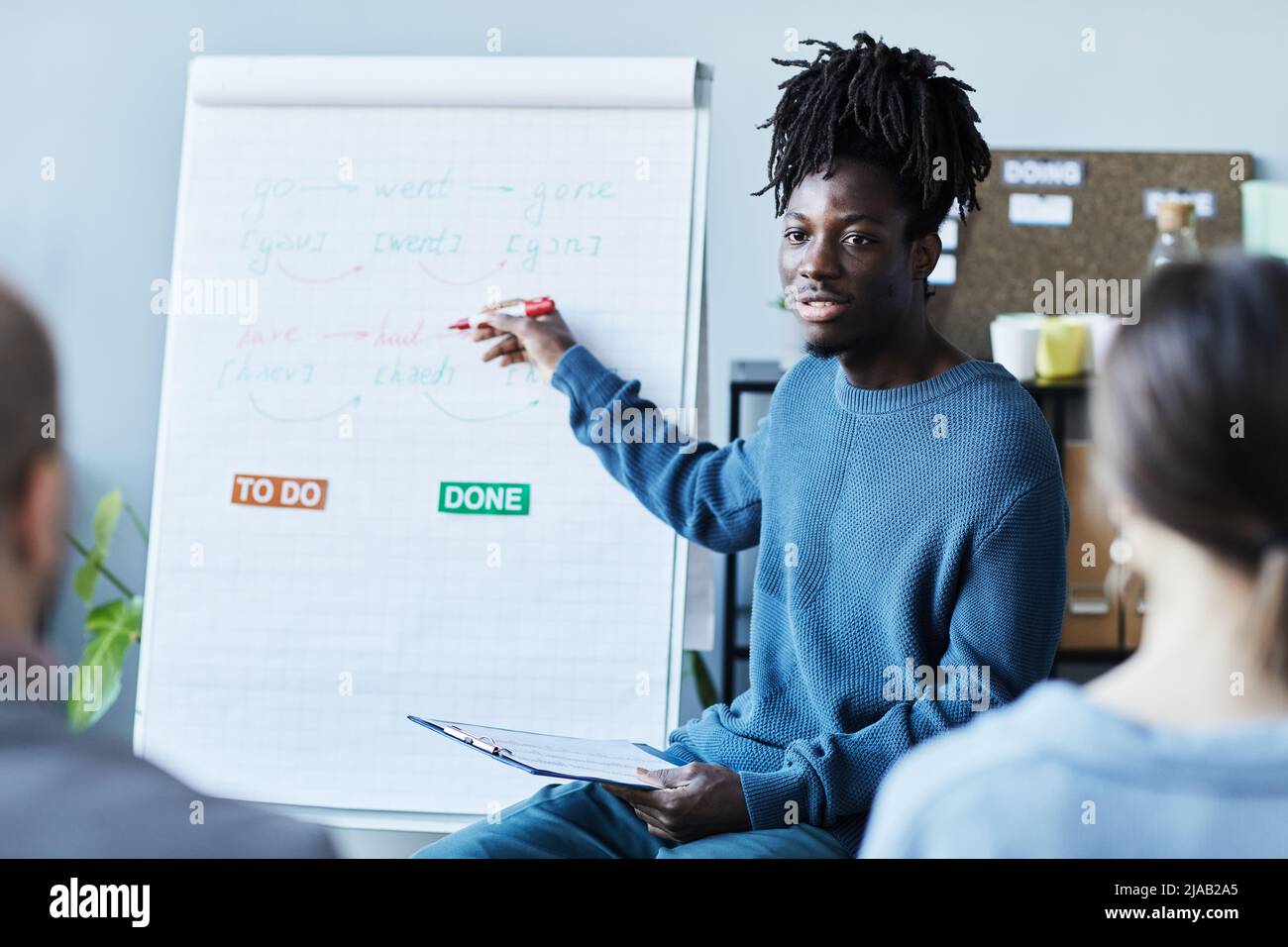Portrait of young black man teaching English class in office to group ...