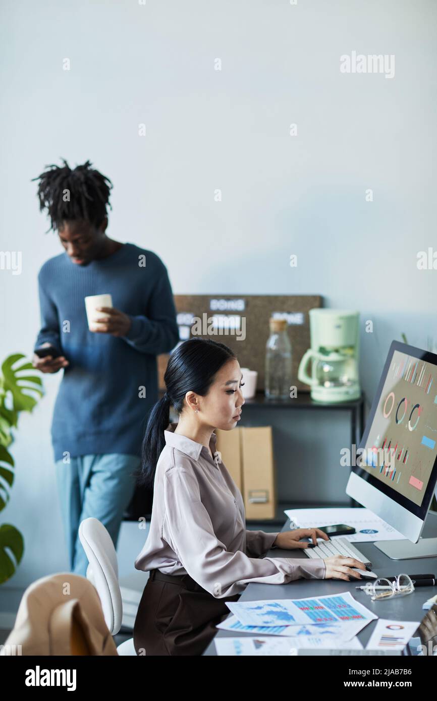 Vertical portrait of diverse team working and operating in company office, focus on Asian young ...