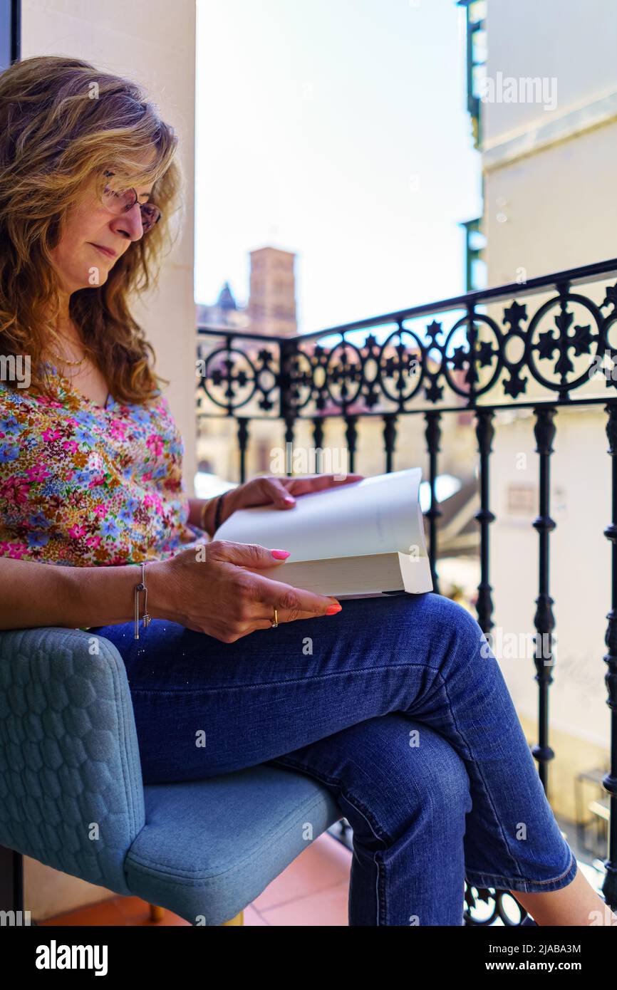 Mature white woman reading a book comfortably on the balcony of her ...