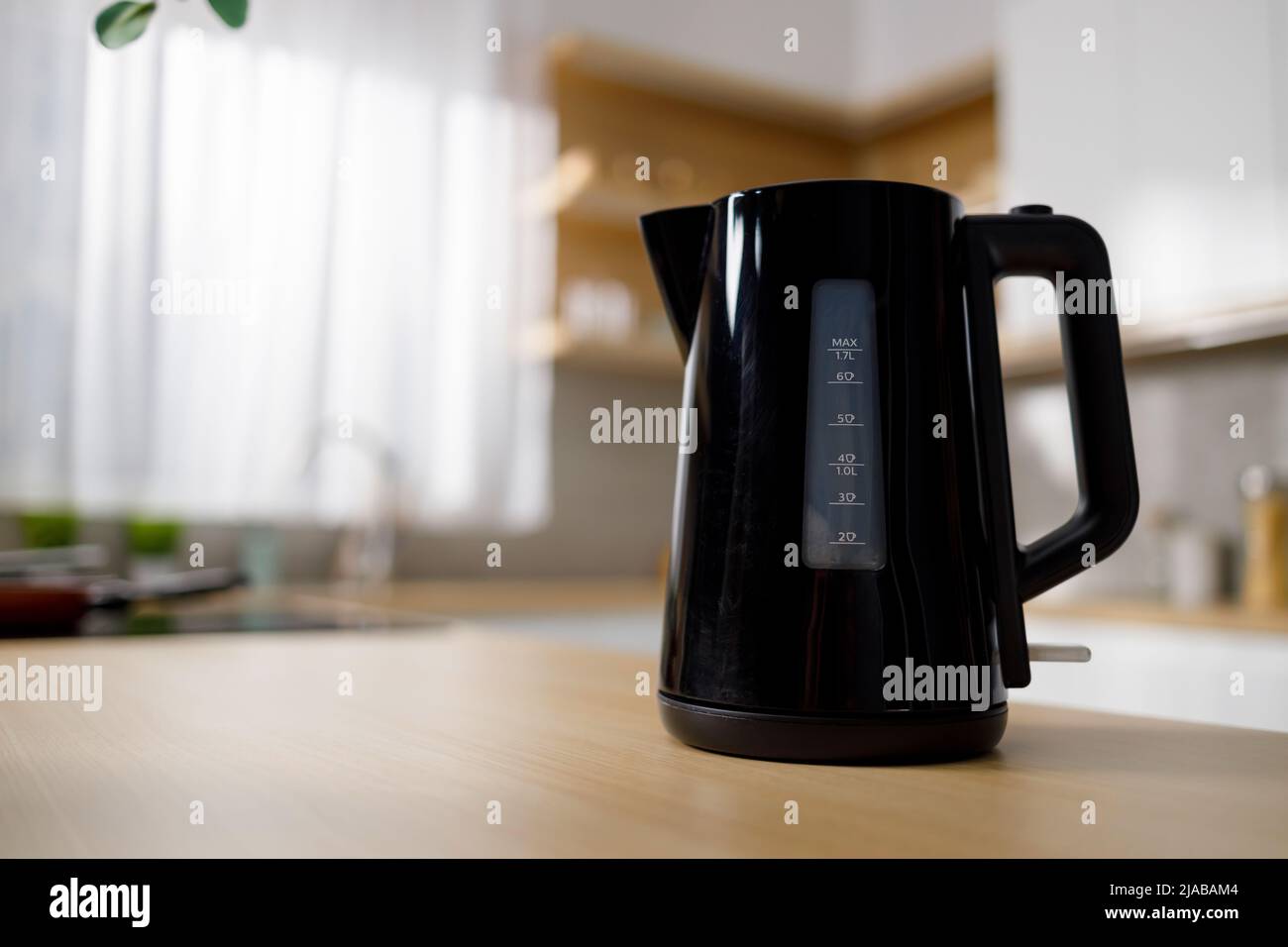 Modern black electric kettle on kitchen table Stock Photo - Alamy