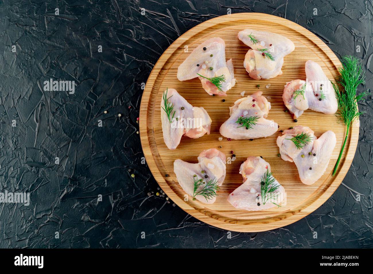 Raw chicken wings lie on a round stand on a black background with ...