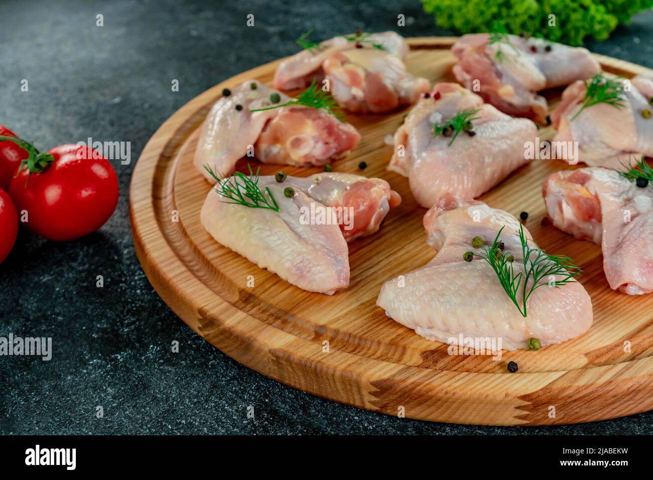 Raw chicken wings lie on a round stand on a black background with ...