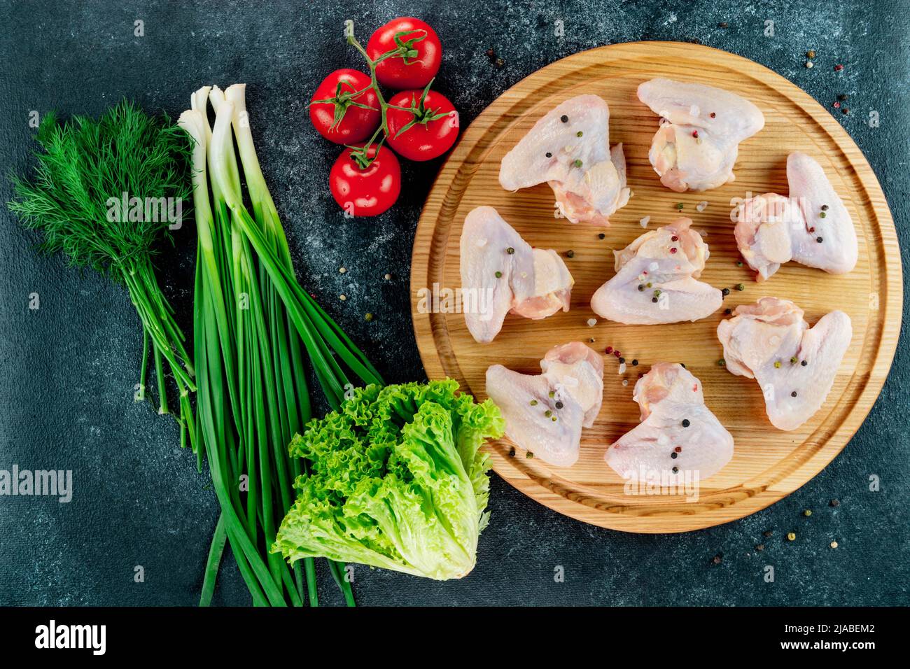 Raw chicken wings lie on a round stand on a black background with ...