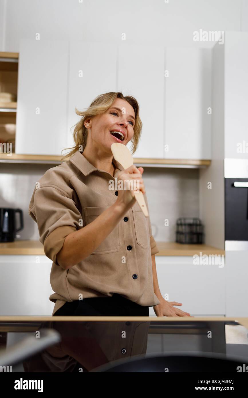 Portrait of a middle-aged woman singing while cooking in the kitchen at ...