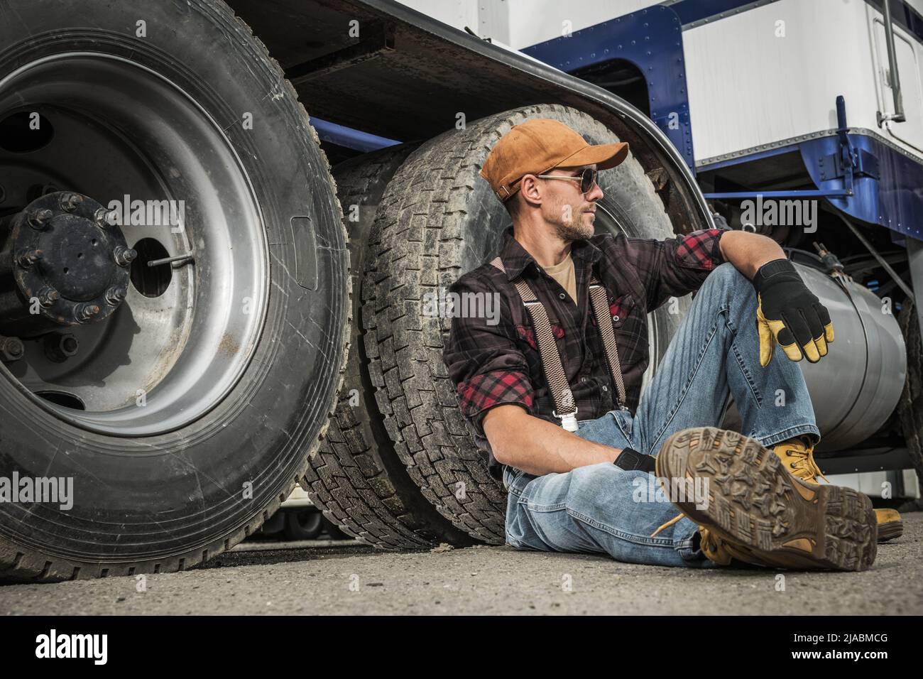 Semi Truck Driver Resting Next to His Truck Seating on a Ground. Heavy ...