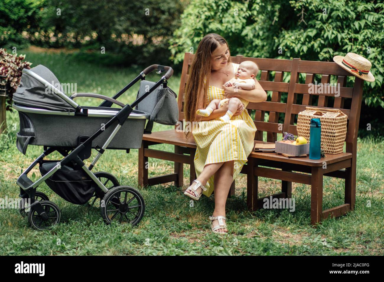 Mother and newborn baby in stroller on summer park. Happy young woman ...
