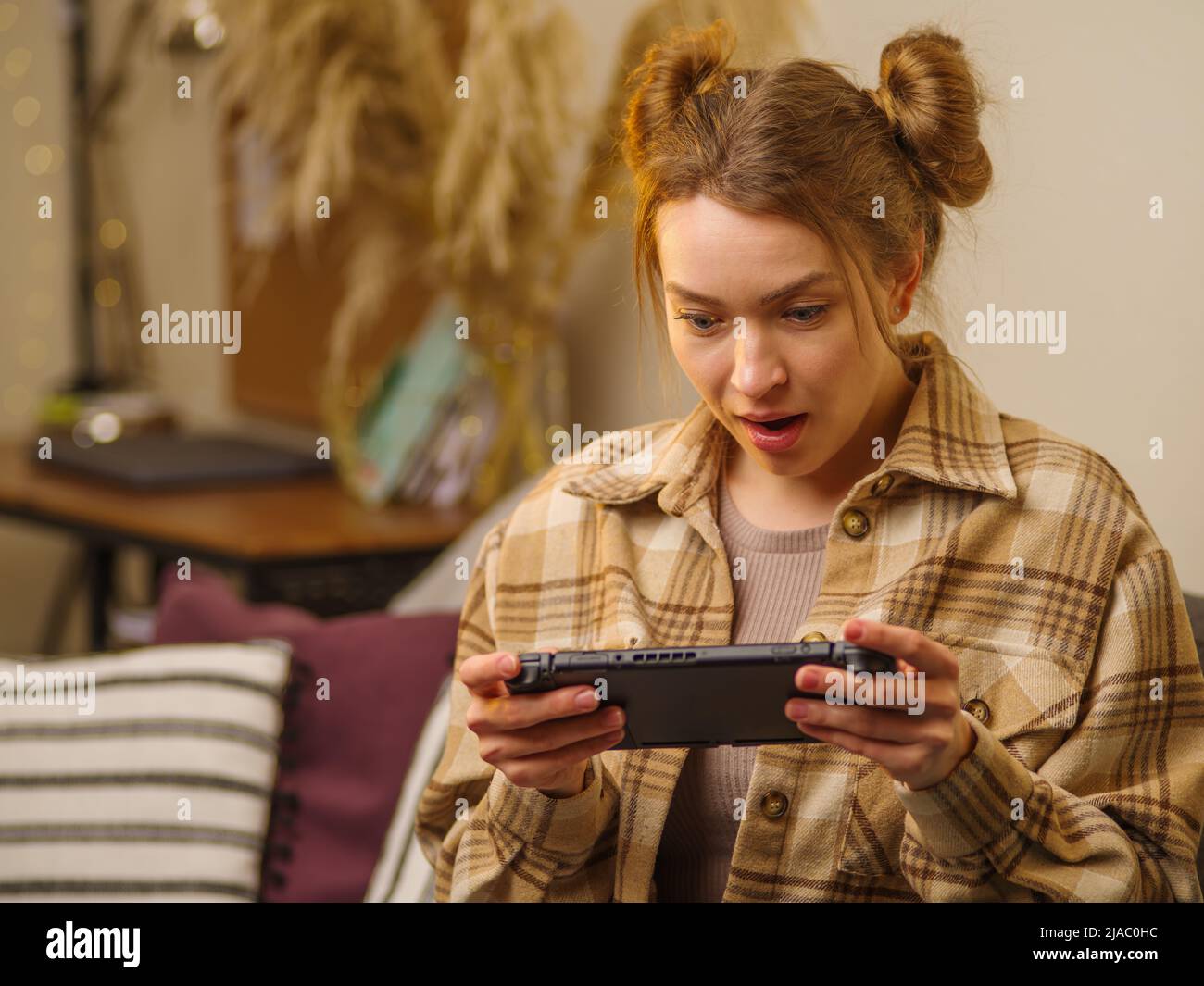 A girl at home in the living room plays video games on a portable game ...