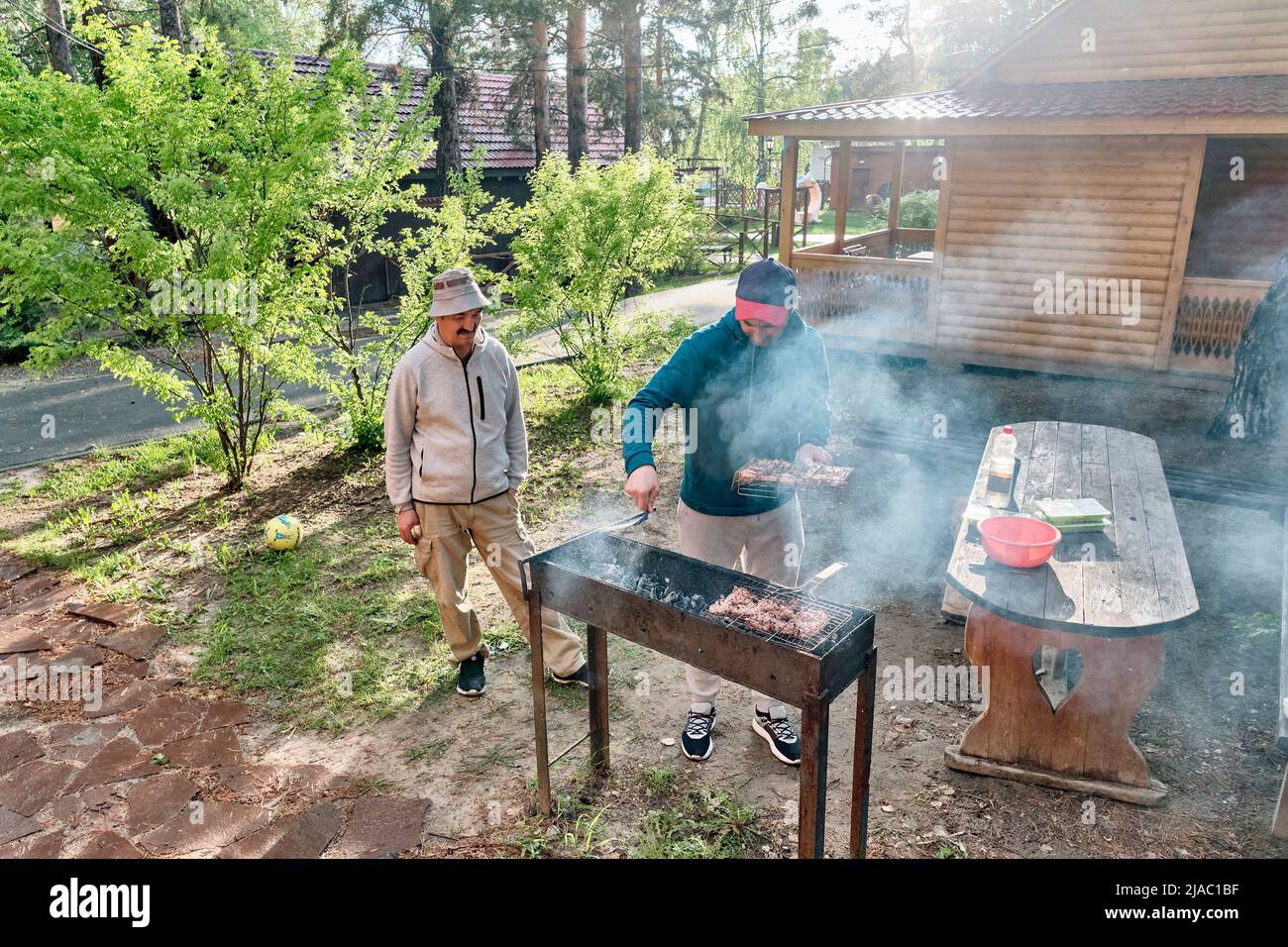 Asian senior man and his adult son cooking meat on barbecue grill in ...