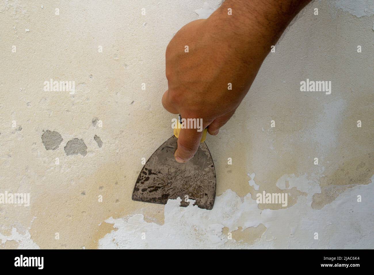 Image of the hands of a handyman who with a metal spatula removes ...