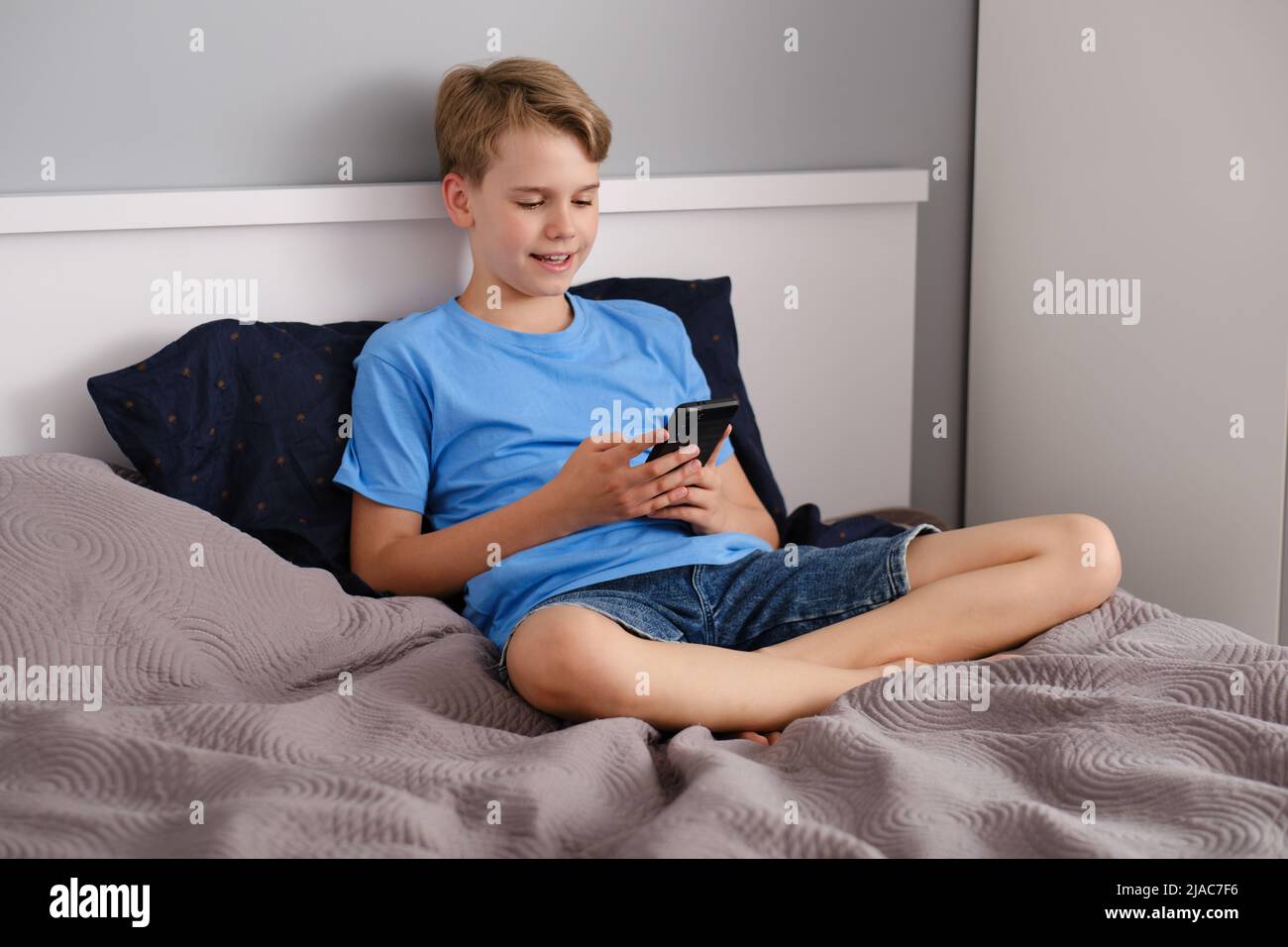 Teen boy uses smartphone for video chat while sitting on bed at home ...