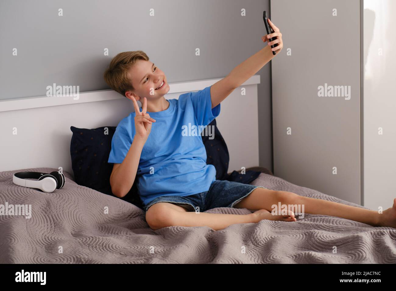 Relaxed happy boy taking selfie or video call while sitting on bed ...