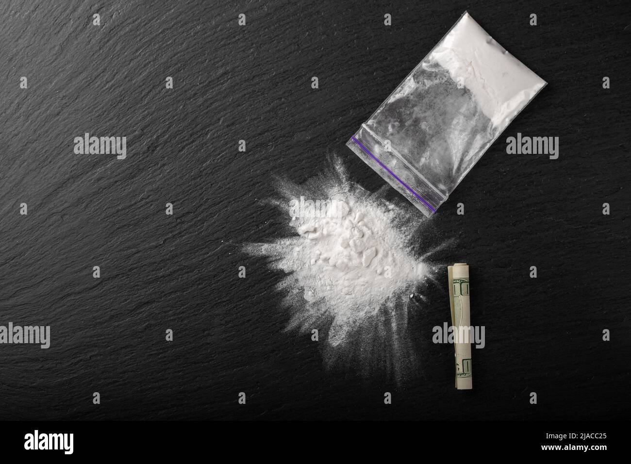 Cocaine in a plastic package on a black background, close-up. A rolled ...