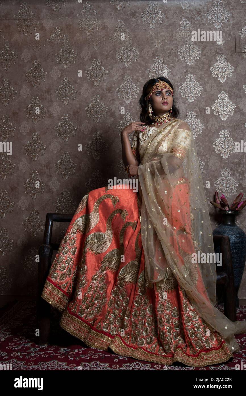 Indian female model wearing an orange and beige lehemga and jewellry ...
