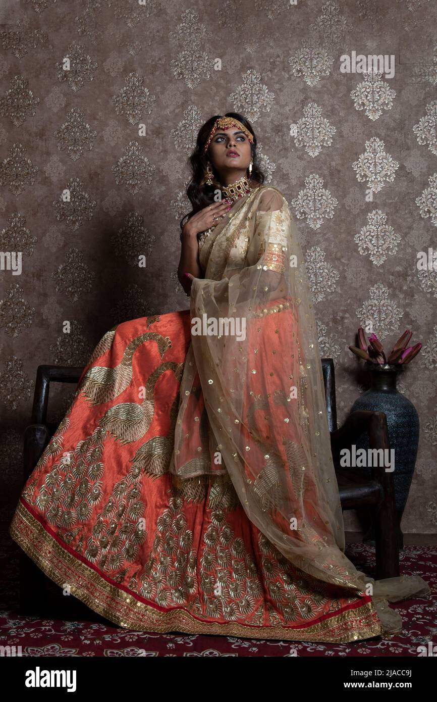 Indian female model wearing an orange and beige lehemga and jewellry ...