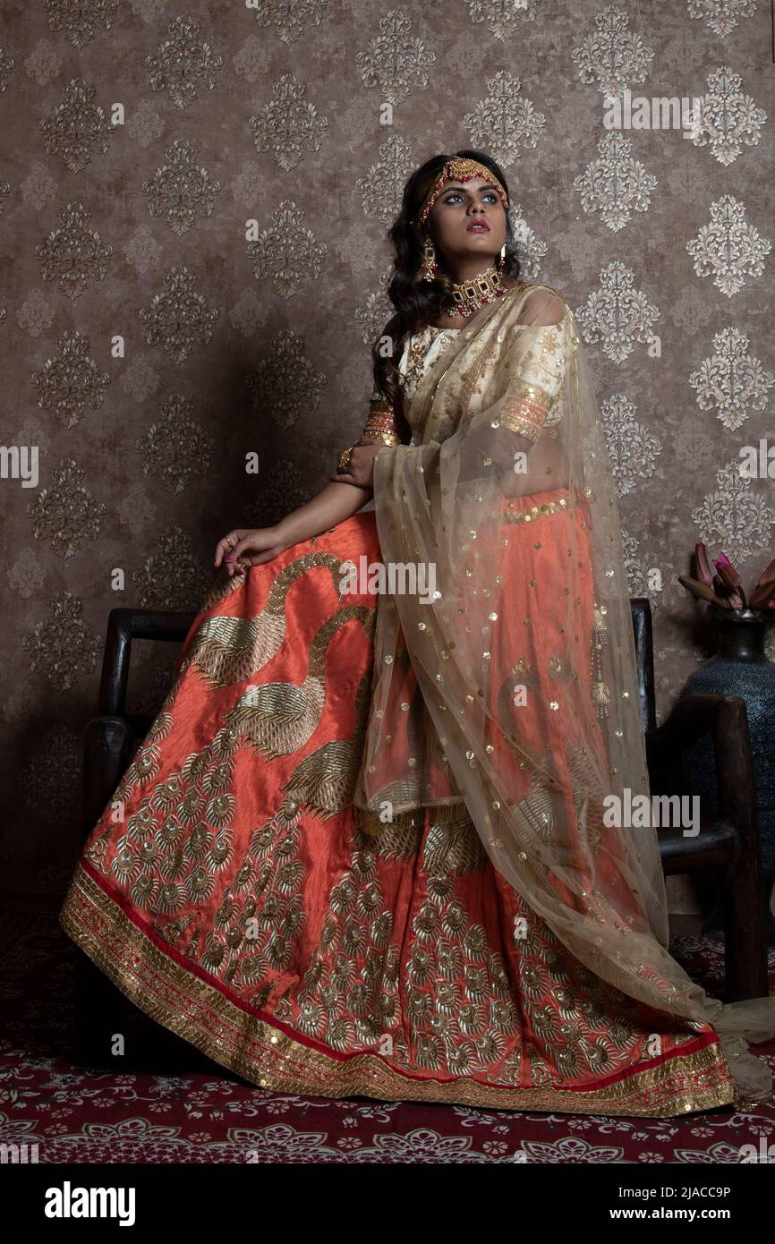 Indian female model wearing an orange and beige lehemga and jewellry ...