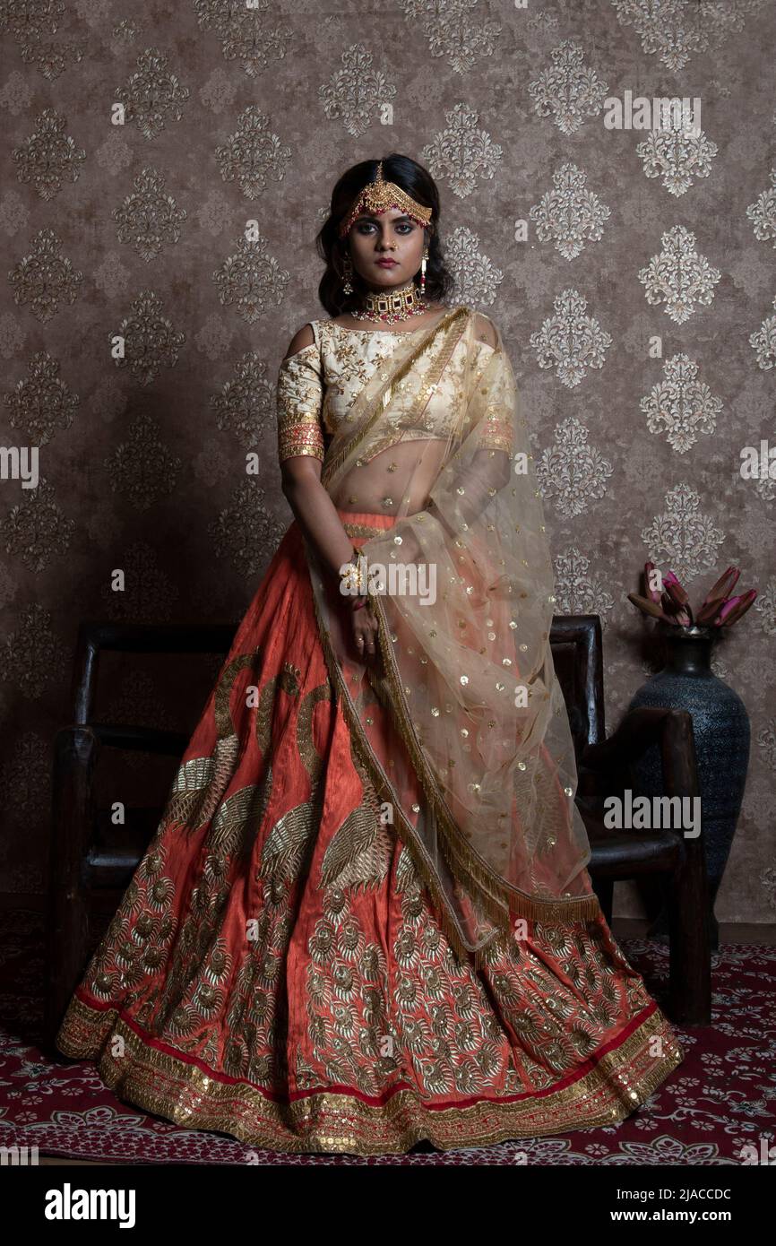 Indian female model wearing an orange and beige lehemga and jewellry ...