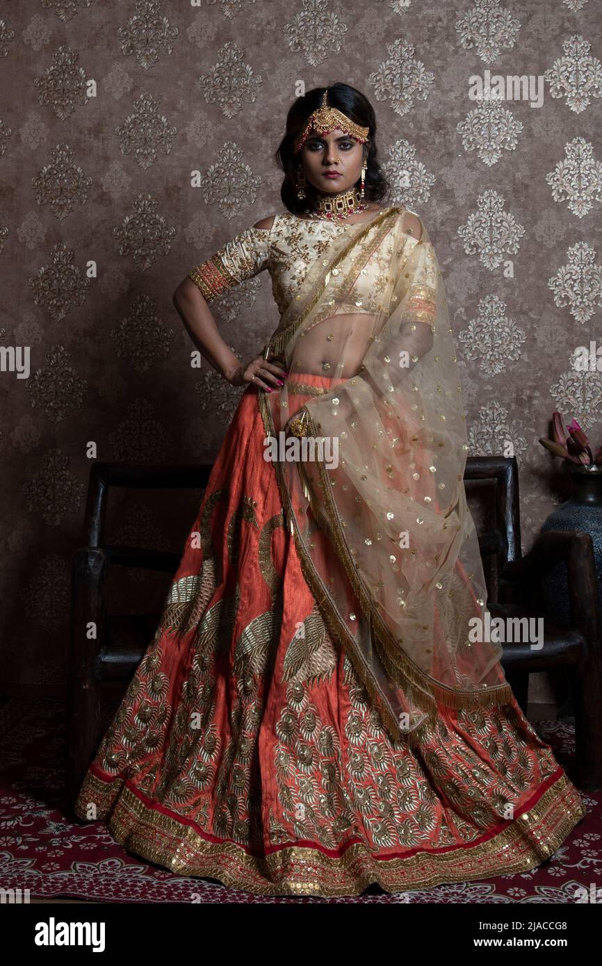 Indian female model wearing an orange and beige lehemga and jewellry ...