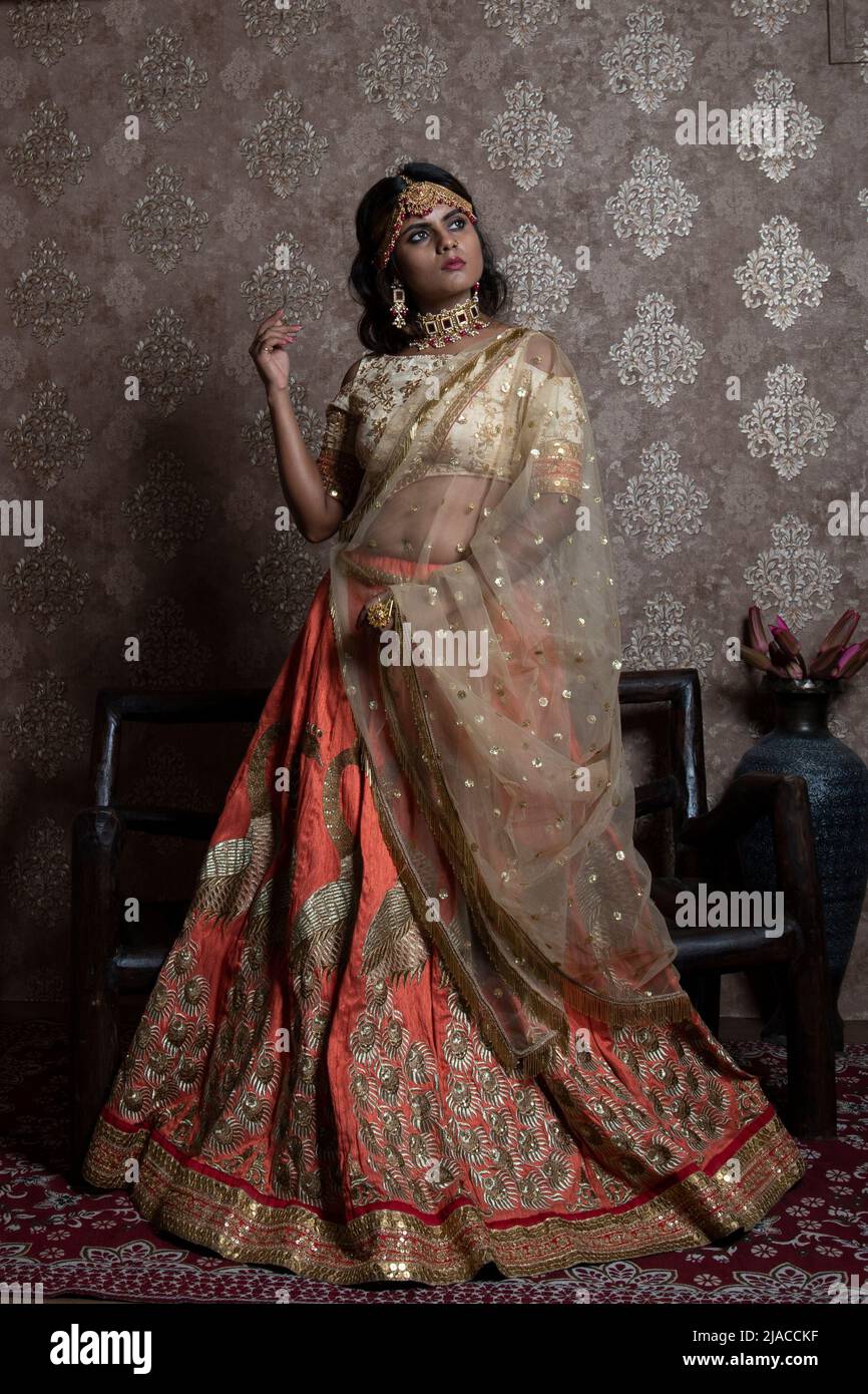 Indian female model wearing an orange and beige lehemga and jewellry ...